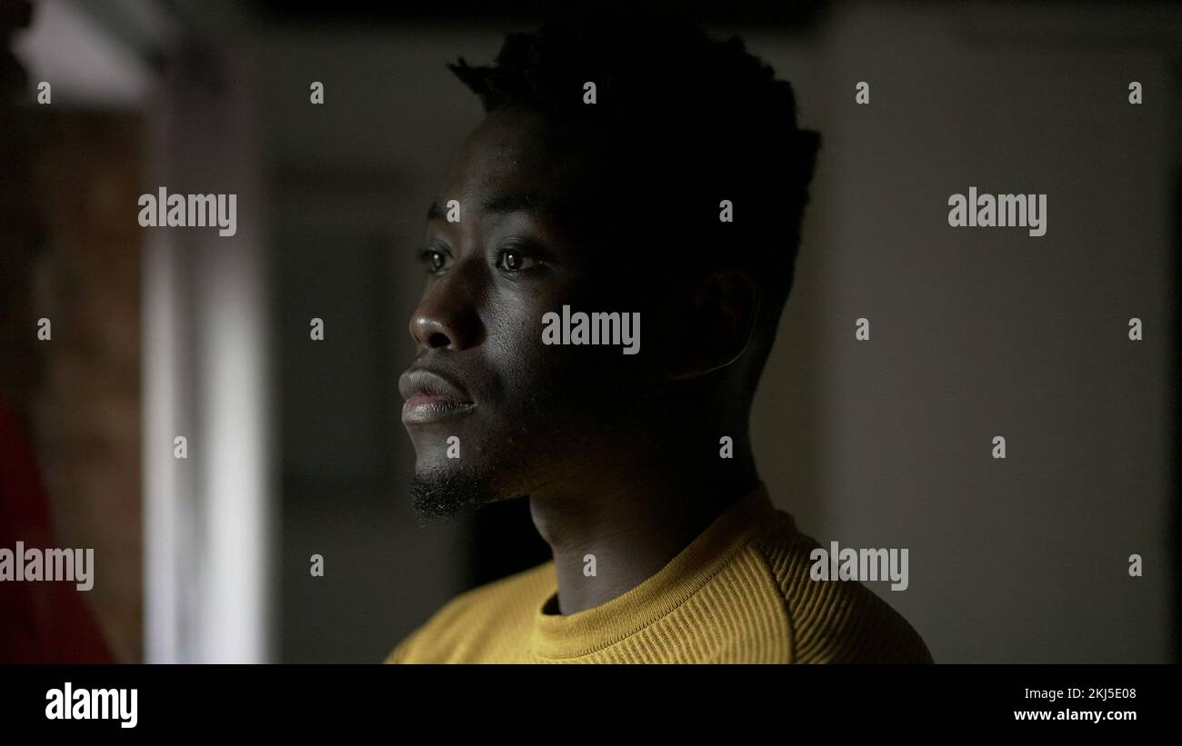 African man standing by window thinking about life. Concerned worried ...