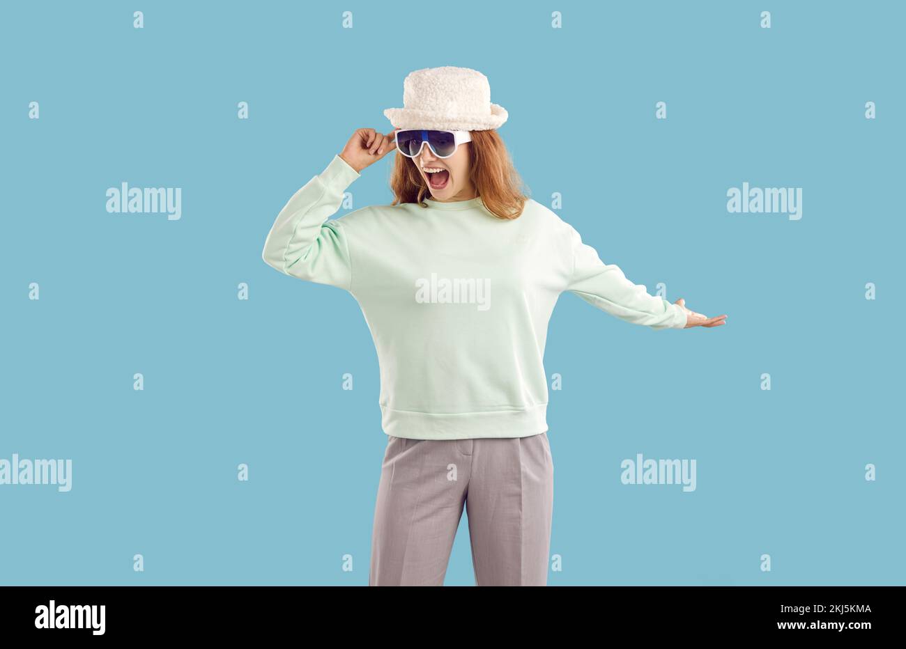 Funny cheerful young woman in hat, sunglasses, mint cotton sweatshirt ...