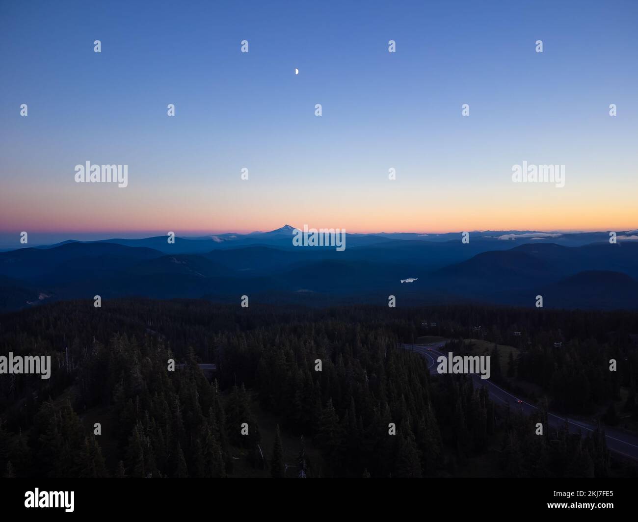 Twilight. Pine forest, mountain range and highway. The sky is colored ...
