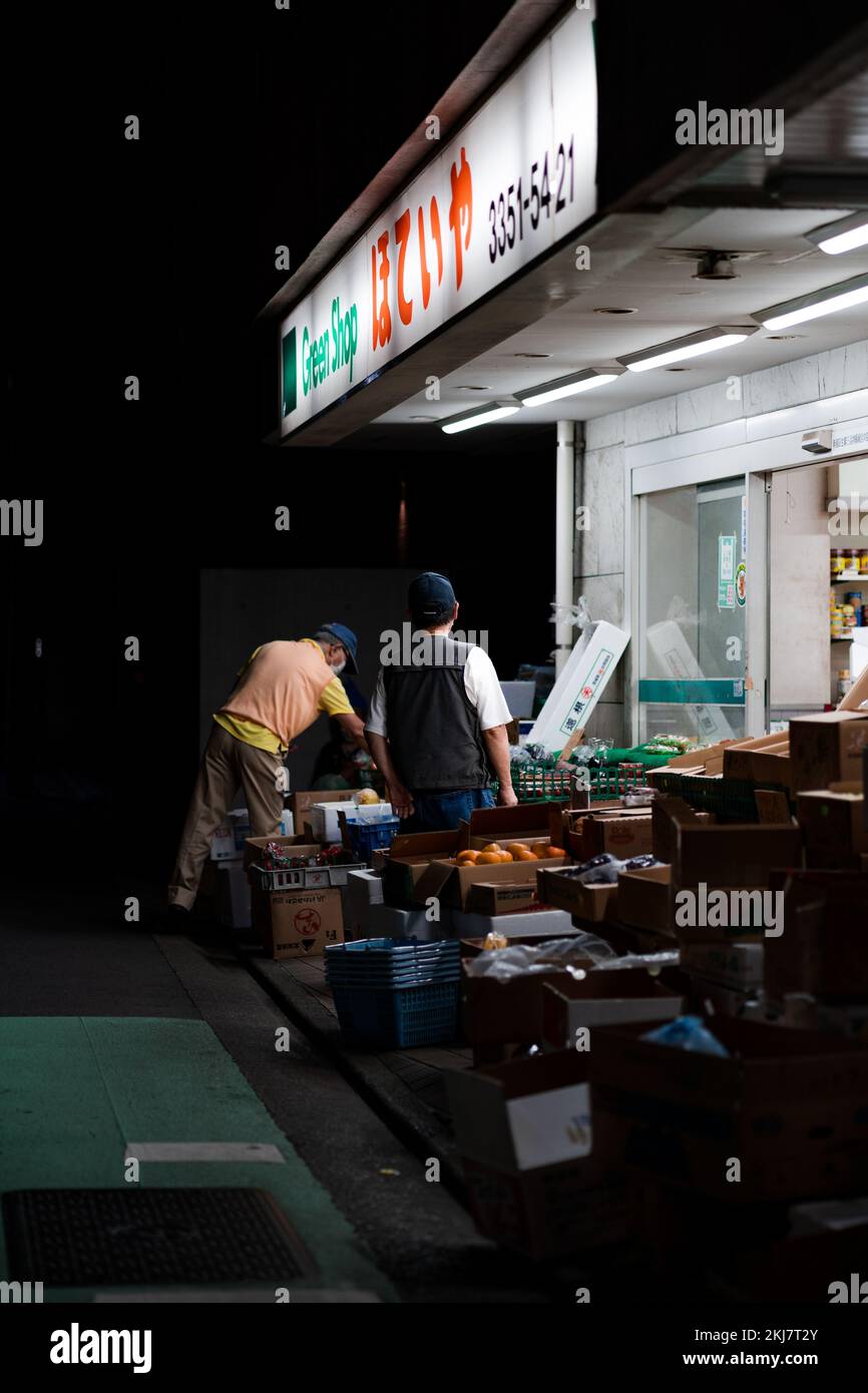 A couple of workers outside a grocery store at night in Tokyo, Japan ...