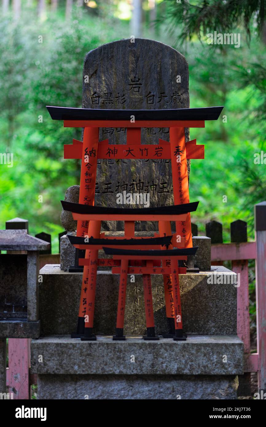 A miniature red torii gate in front of an inscribed stone shrine in the ...
