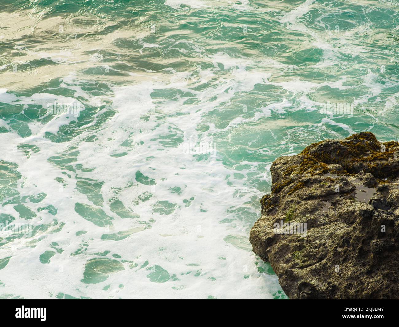 Big boulder in the ocean. Turquoise water with white foamy waves beats ...