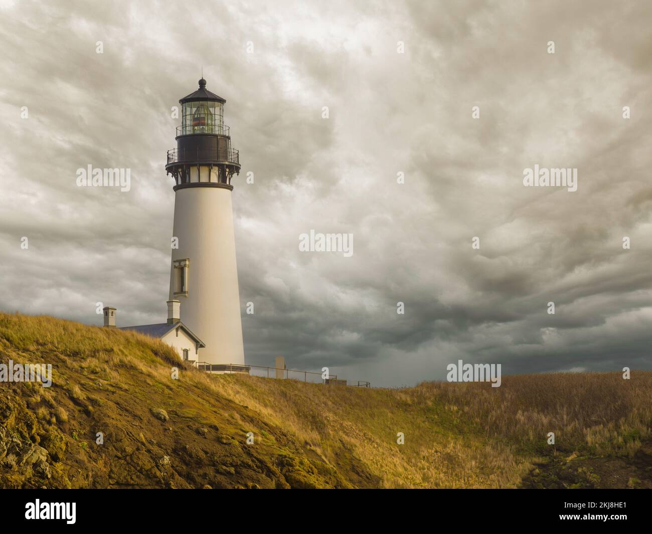 A white high lighthouse on the green shore of the ocean against the ...
