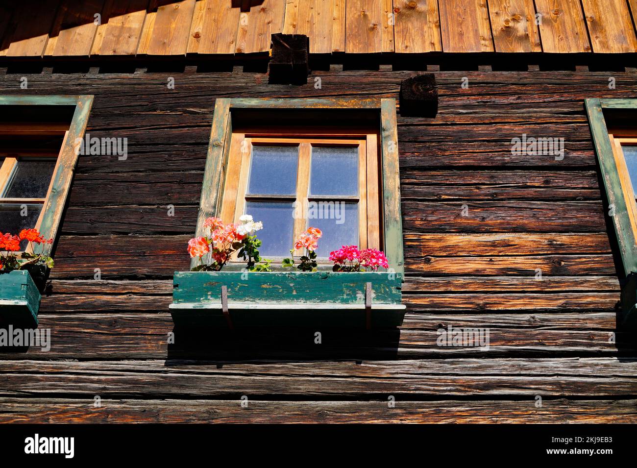 rustic alpine cabin or log cabin with geraniums on the window ledge in ...