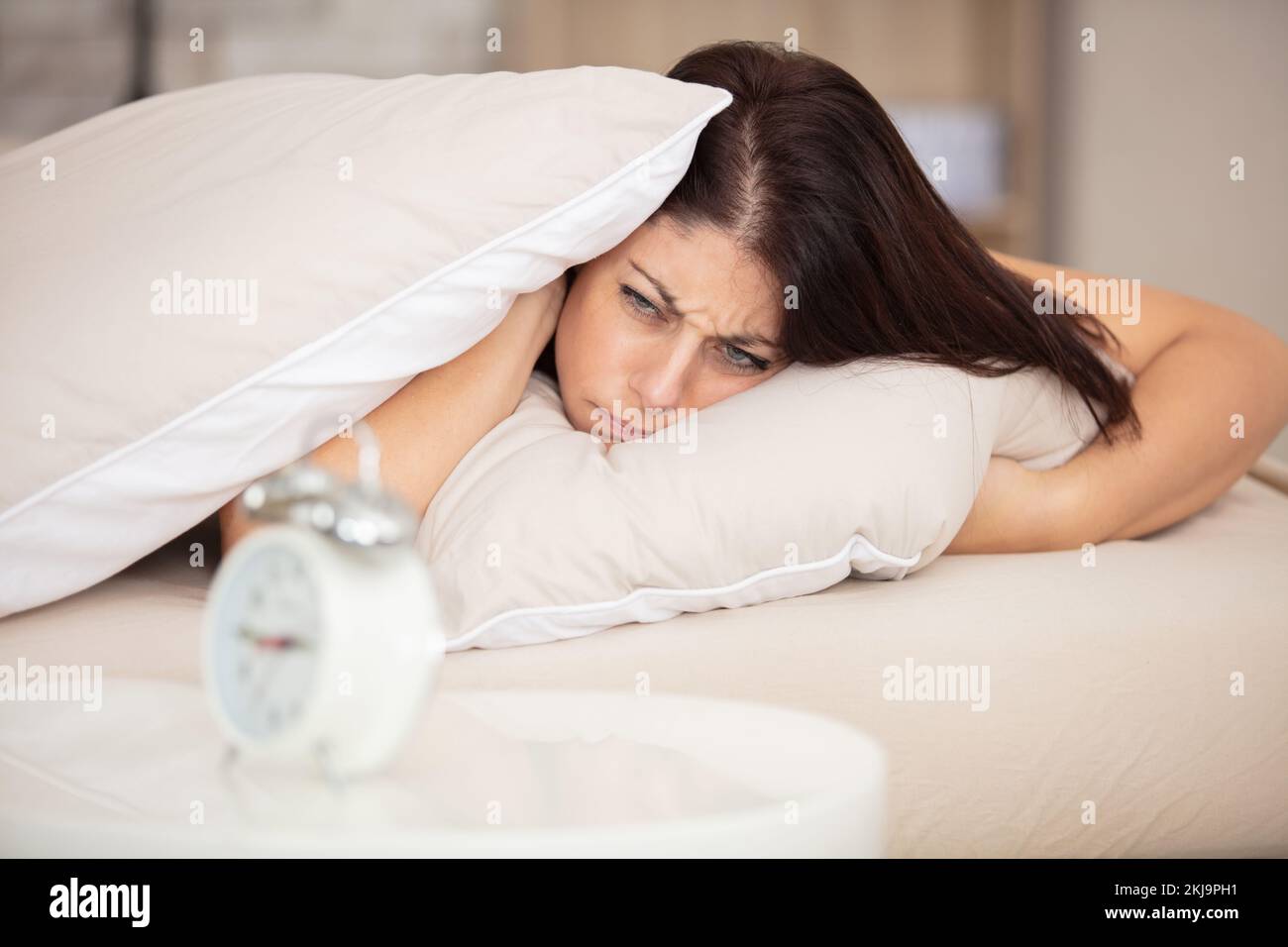 woman in bed covering ears from alarm clock noise Stock Photo - Alamy