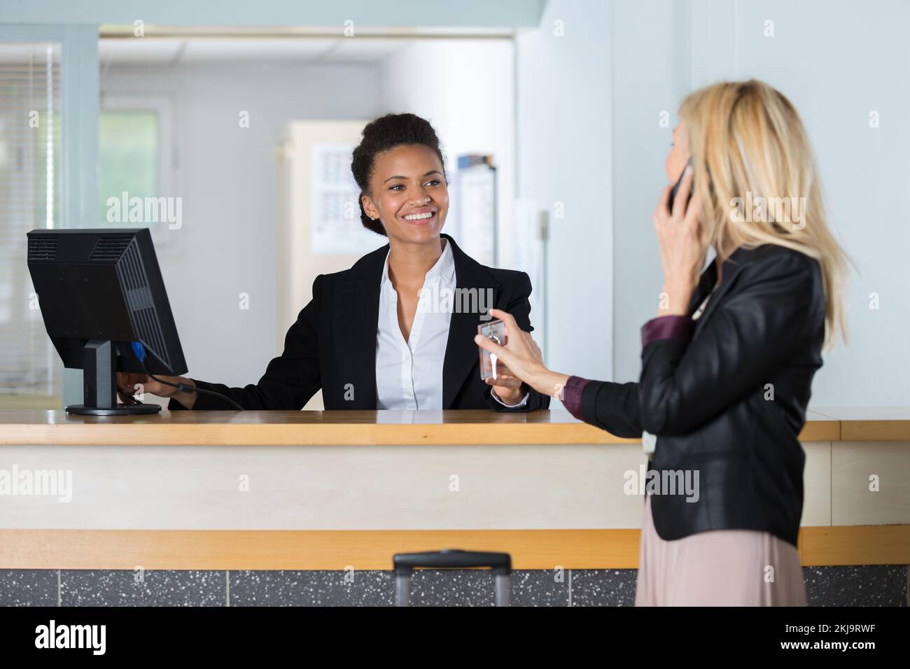hotel receptionist passing keys to female client talking on smartphone ...
