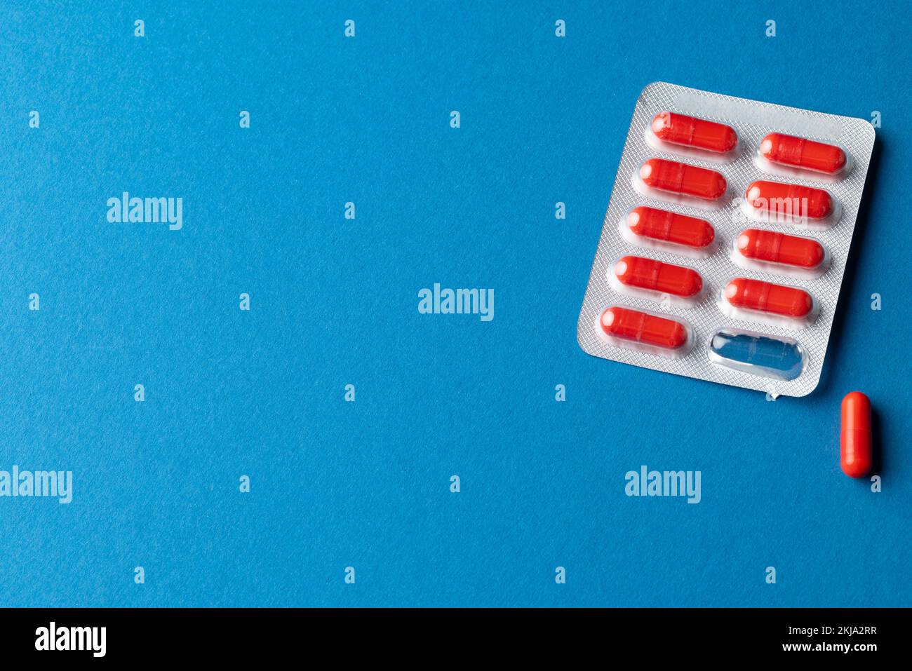 Composition of red pills in blister pack, and one pill out, on blue ...