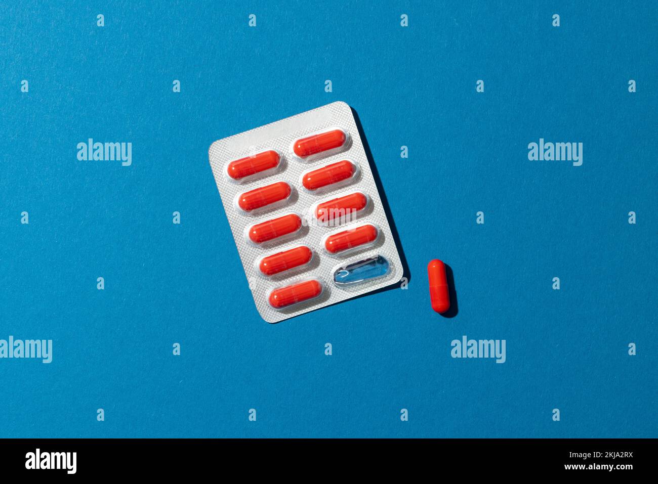 Composition of red pills in blister pack, and one pill out, on blue ...