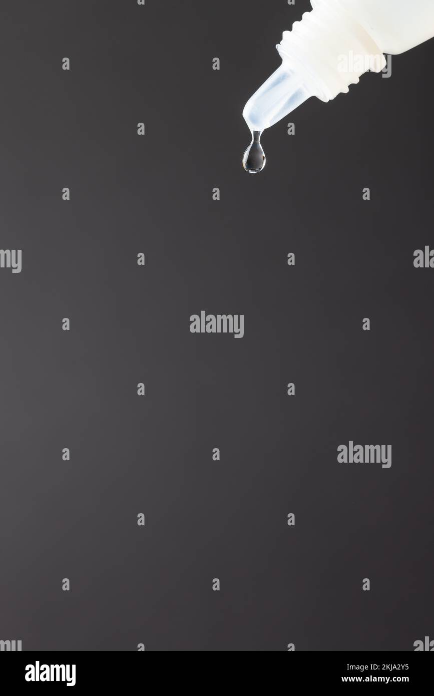 Vertical composition of drop falling from white dropper bottle on black ...