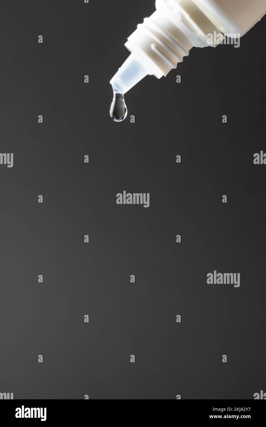 Vertical composition of drop falling from white dropper bottle on black ...