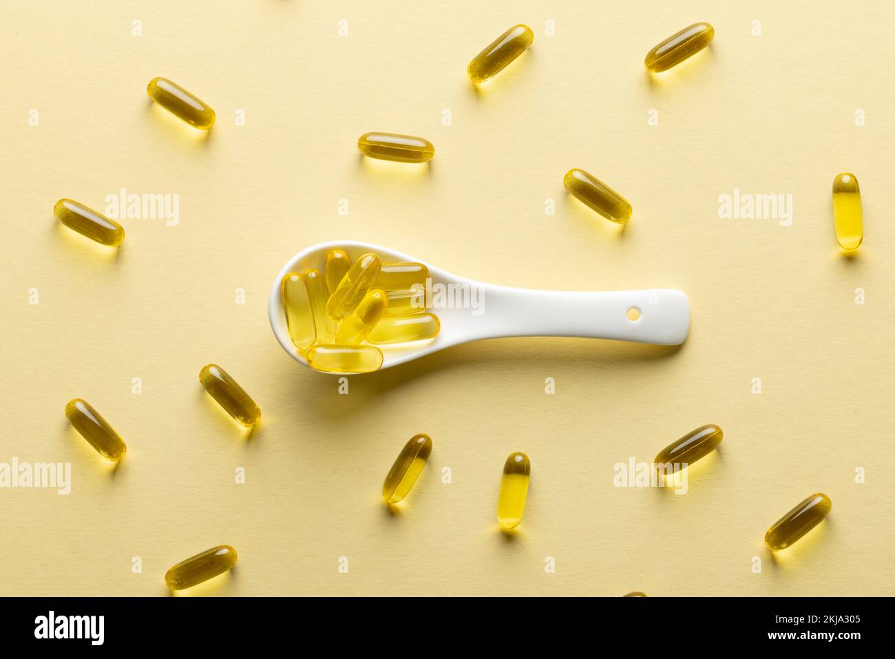 Composition of oil capsules and white spoon on yellow background Stock ...
