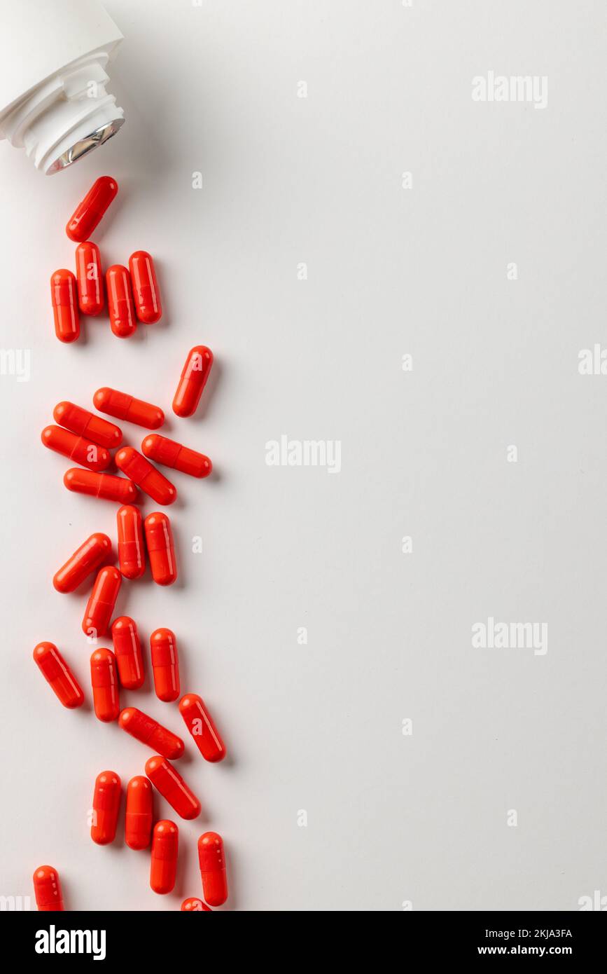 Vertical composition of white pill box spilling red pills on white ...