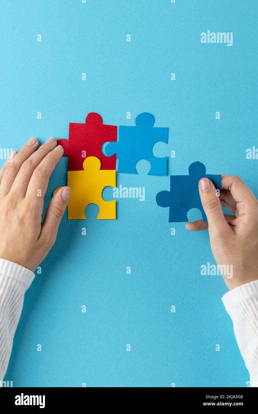 Vertical of hands putting jigsaw puzzle pieces together on blue ...