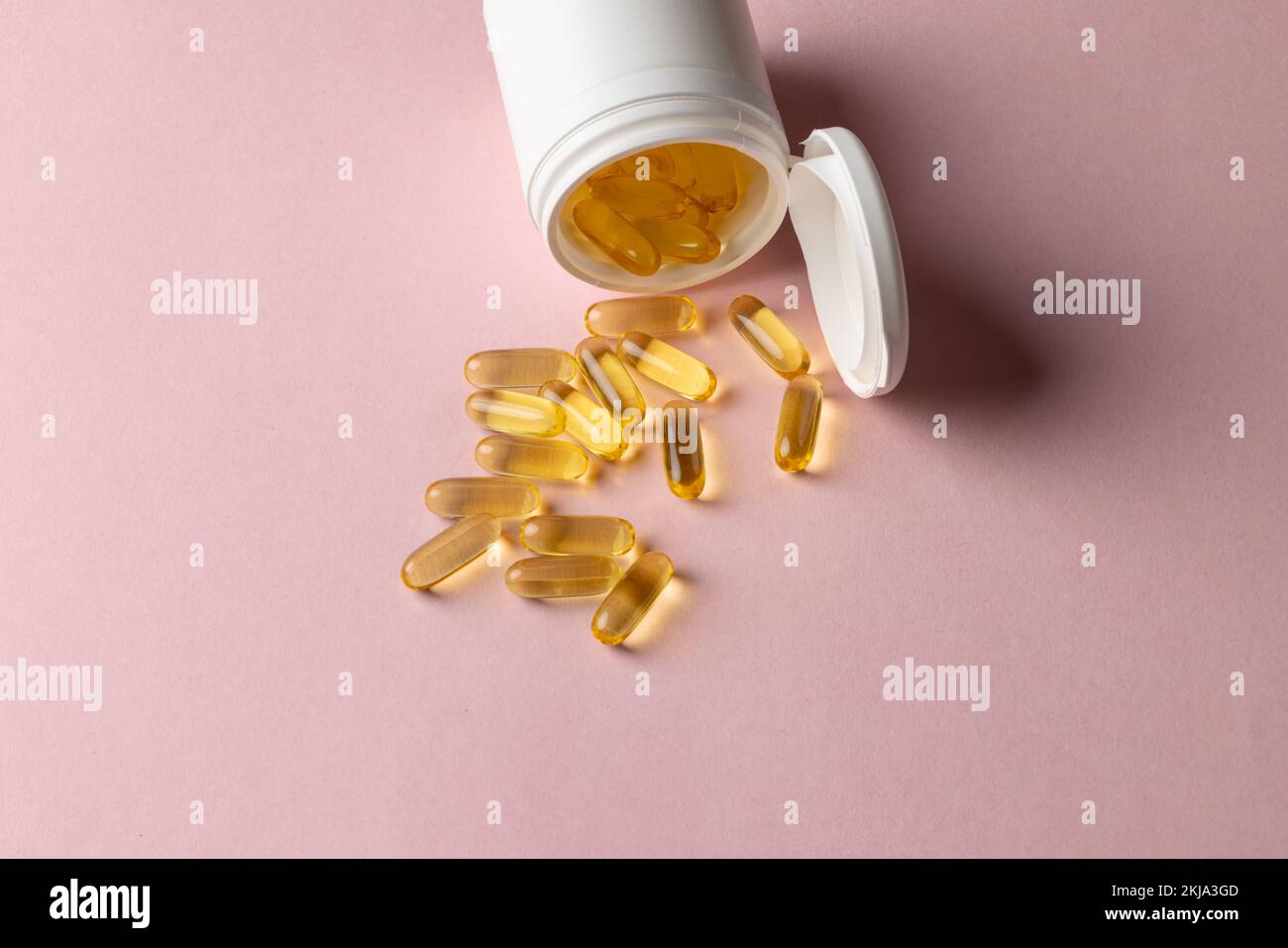 Composition of white pill box spilling oil capsules on pink background ...