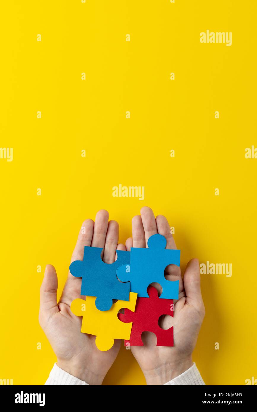 Vertical composition of hands holding jigsaw puzzle pieces on yellow ...