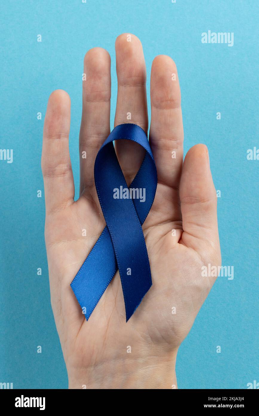 Vertical of hand holding blue colon cancer awareness ribbon on blue ...