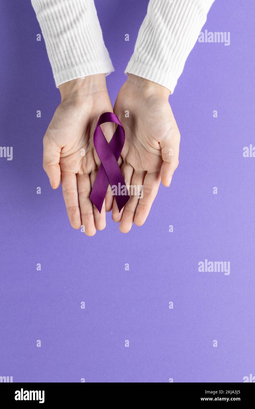Vertical of hands holding purple cancer awareness ribbon on purple ...
