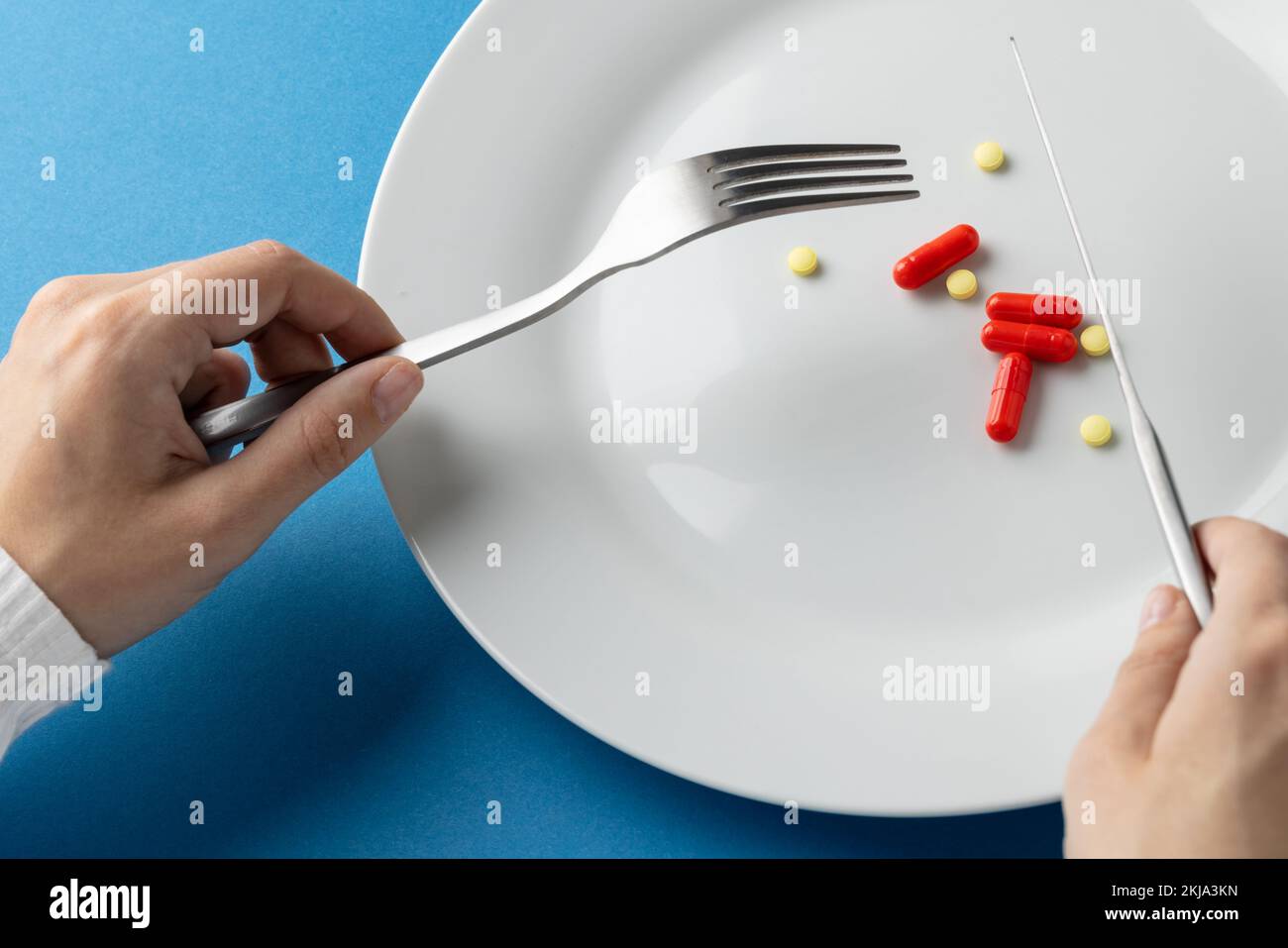 Composition of hands holding fork and knife over plate with pills, on ...
