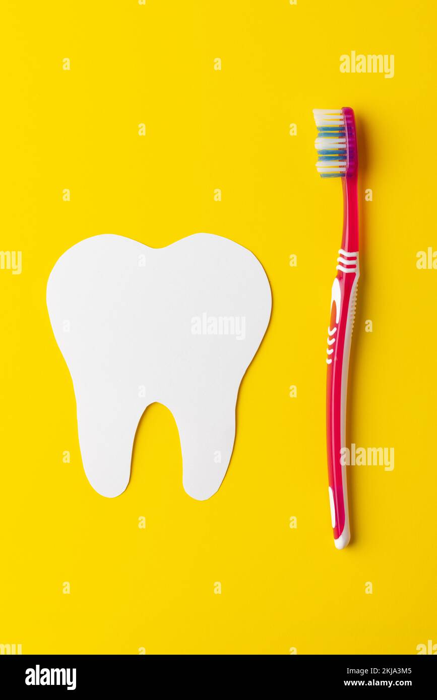 Vertical composition of white tooth and toothbrush on yellow background ...
