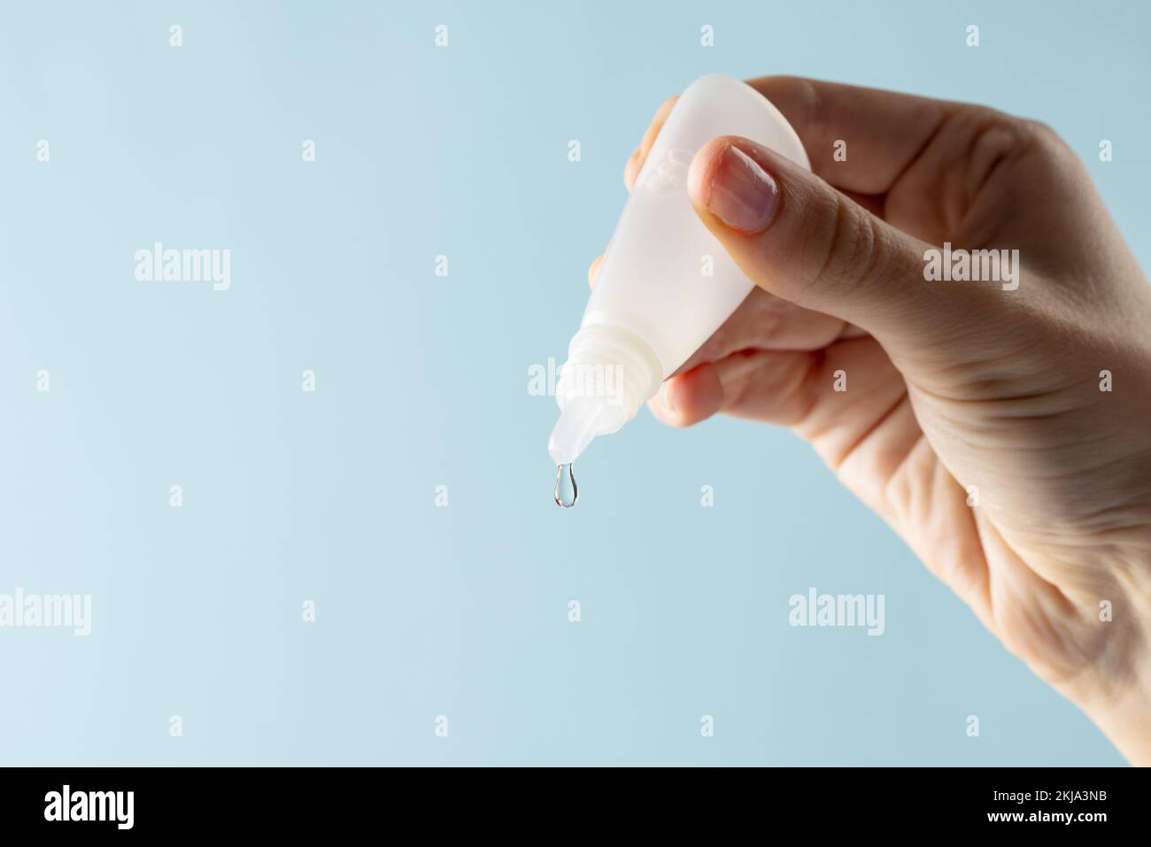 Composition of hand holding dropper bottle with falling drop, on blue ...