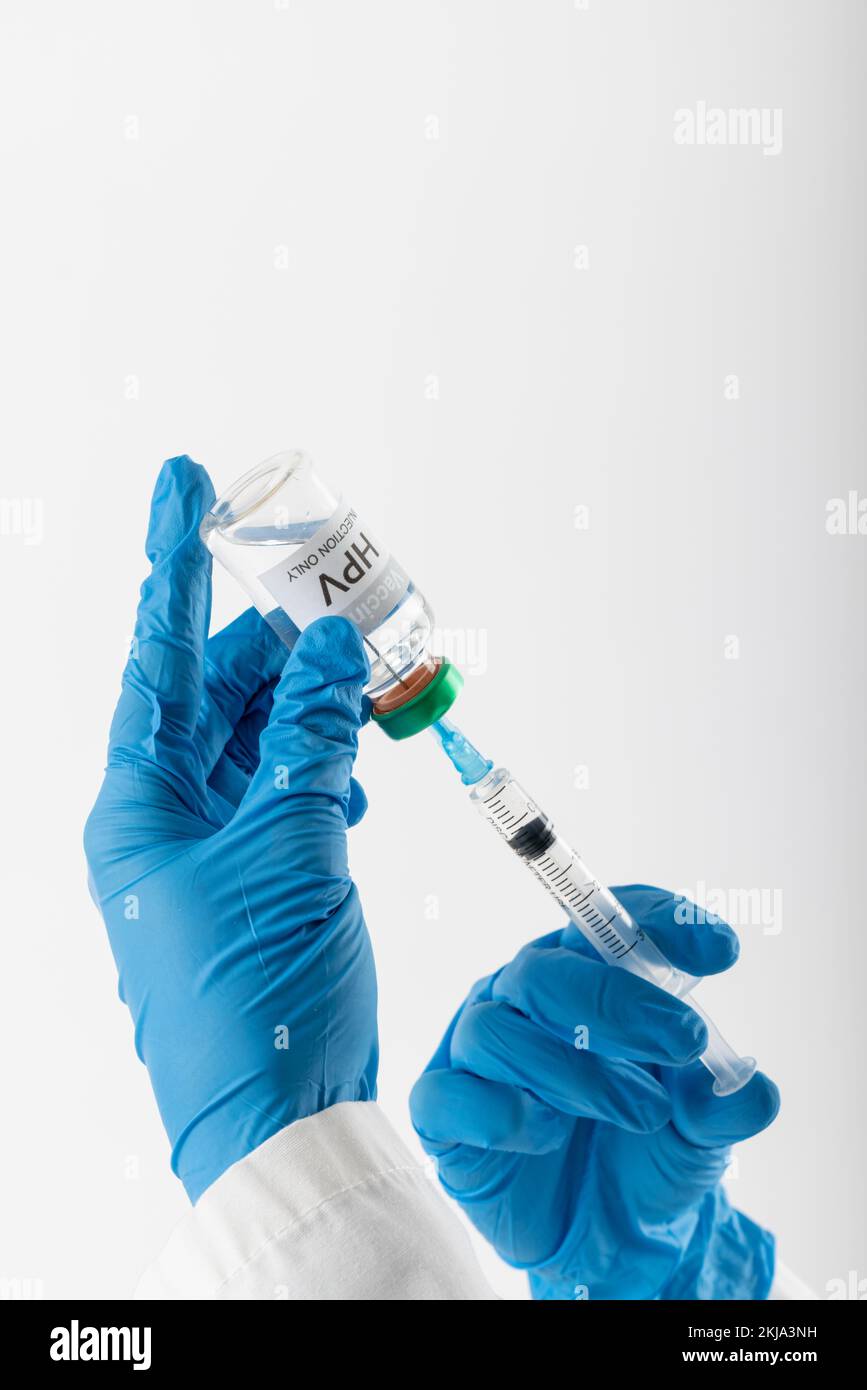 Vertical of doctor's gloved hands filling syringe from hpv vaccine vial ...