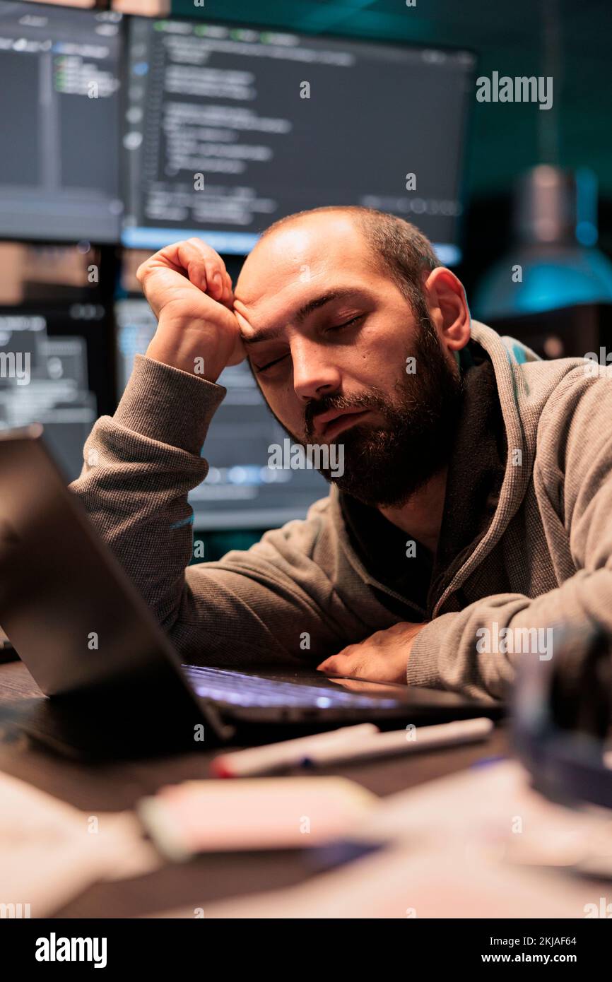 Tired IT enigneer falling asleep at office desk working on interface programming, holding head ...