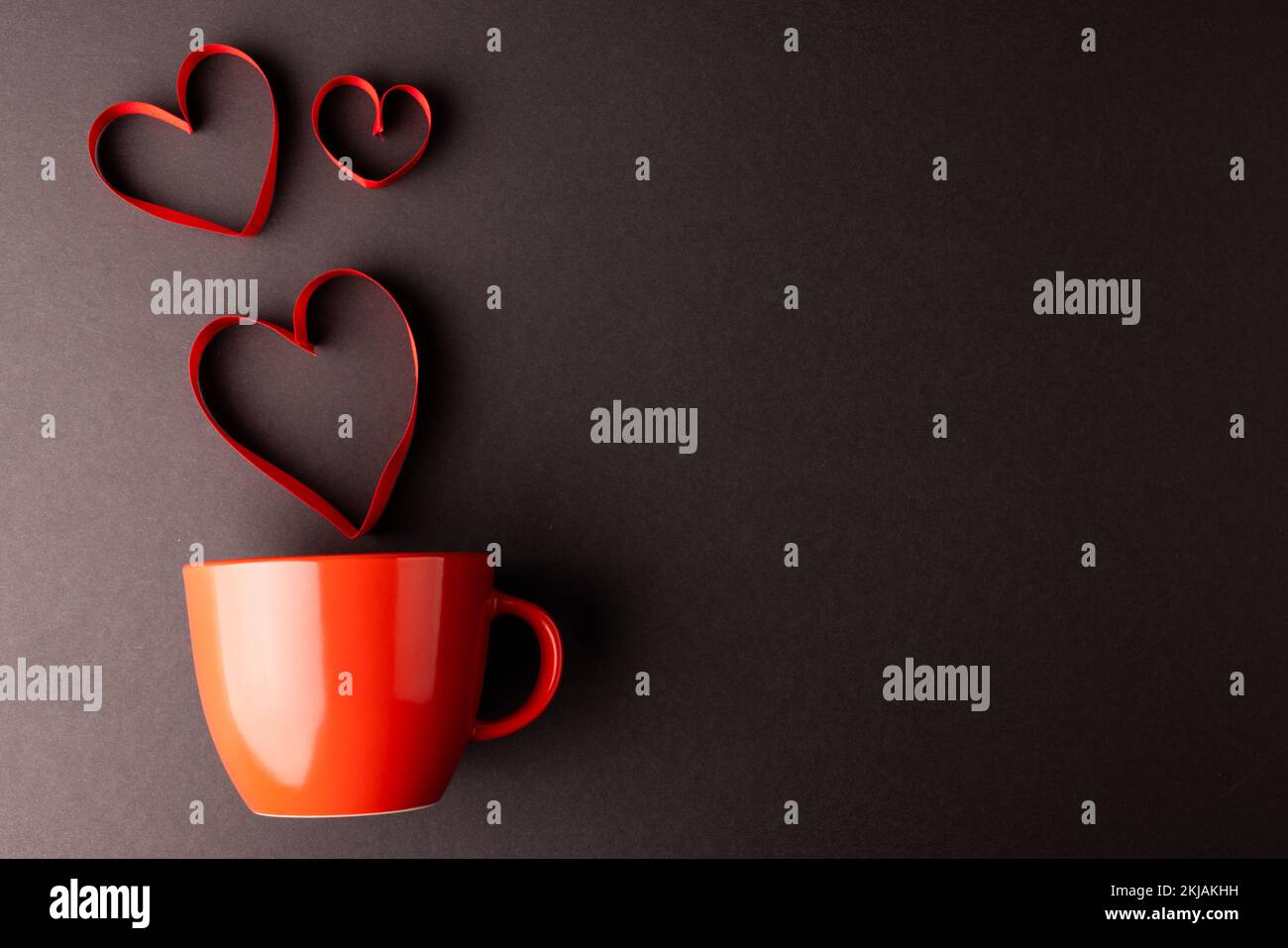 Red heart shapes rising from red mug on dark grey background, with copy ...