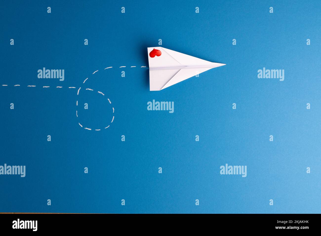 Paper plane with red heart and white trail, on blue background with ...