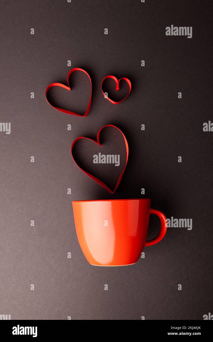 Vertical of red heart shapes rising from red mug on dark grey ...