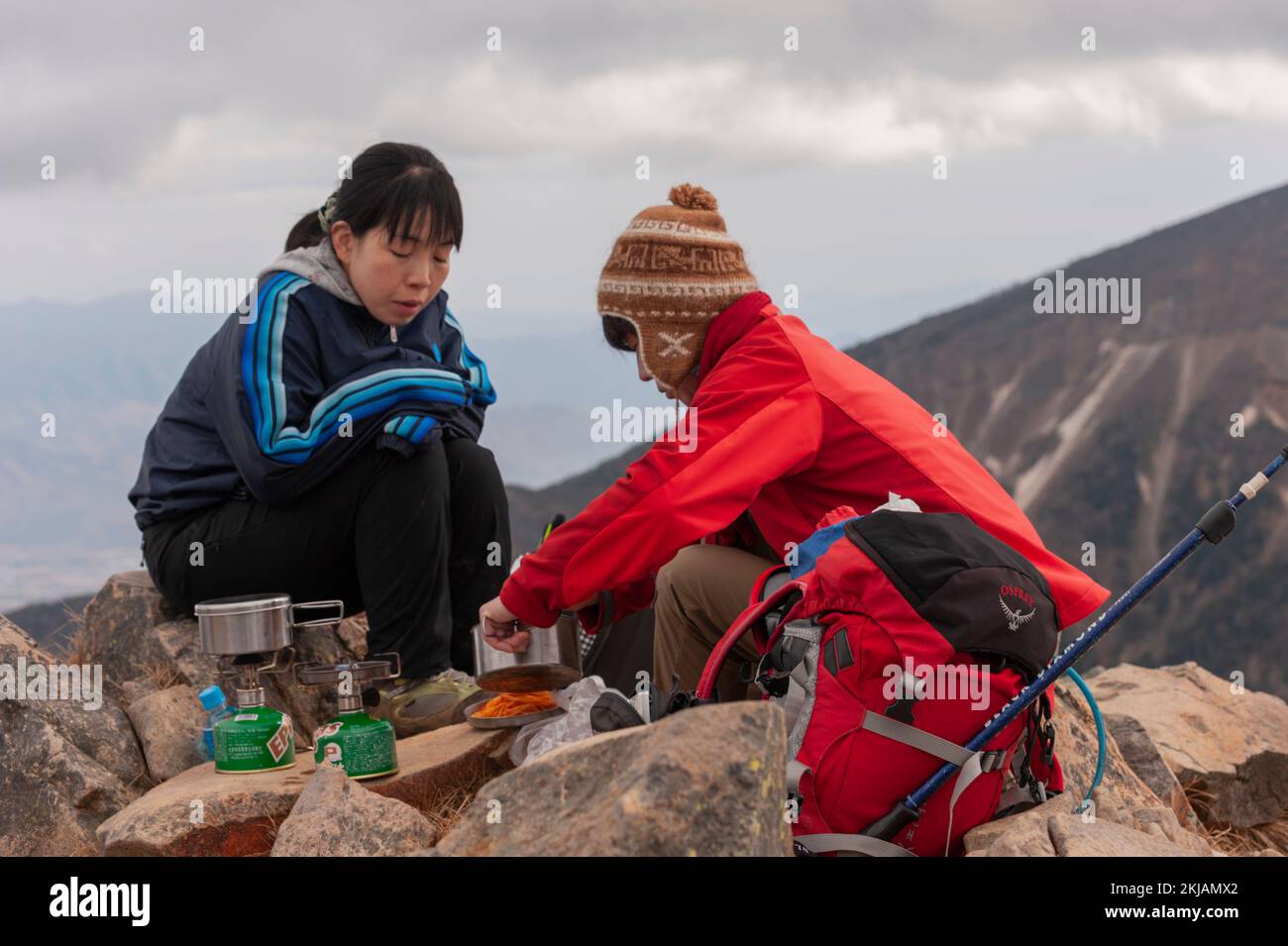 Two women mountain climbers cook spaghetti for lunch atop a rocky peak ...