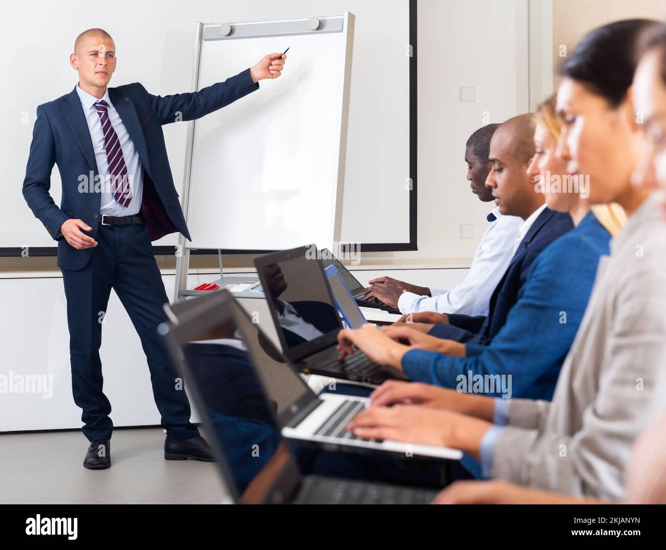 Businessman presenting project to team members sitting with laptops ...