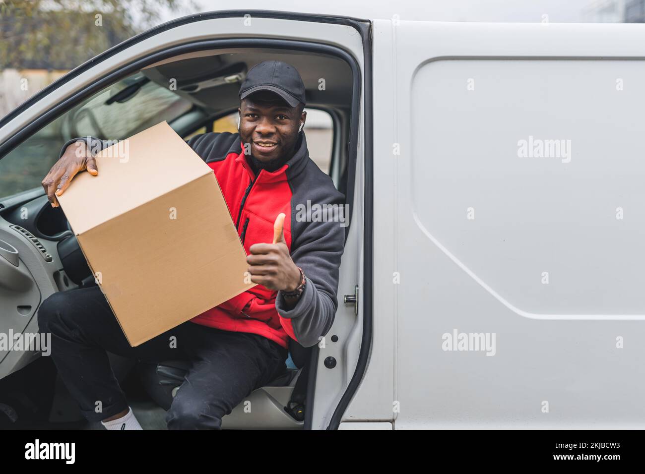 Young adult black delivery man getting out of white van with carboard ...