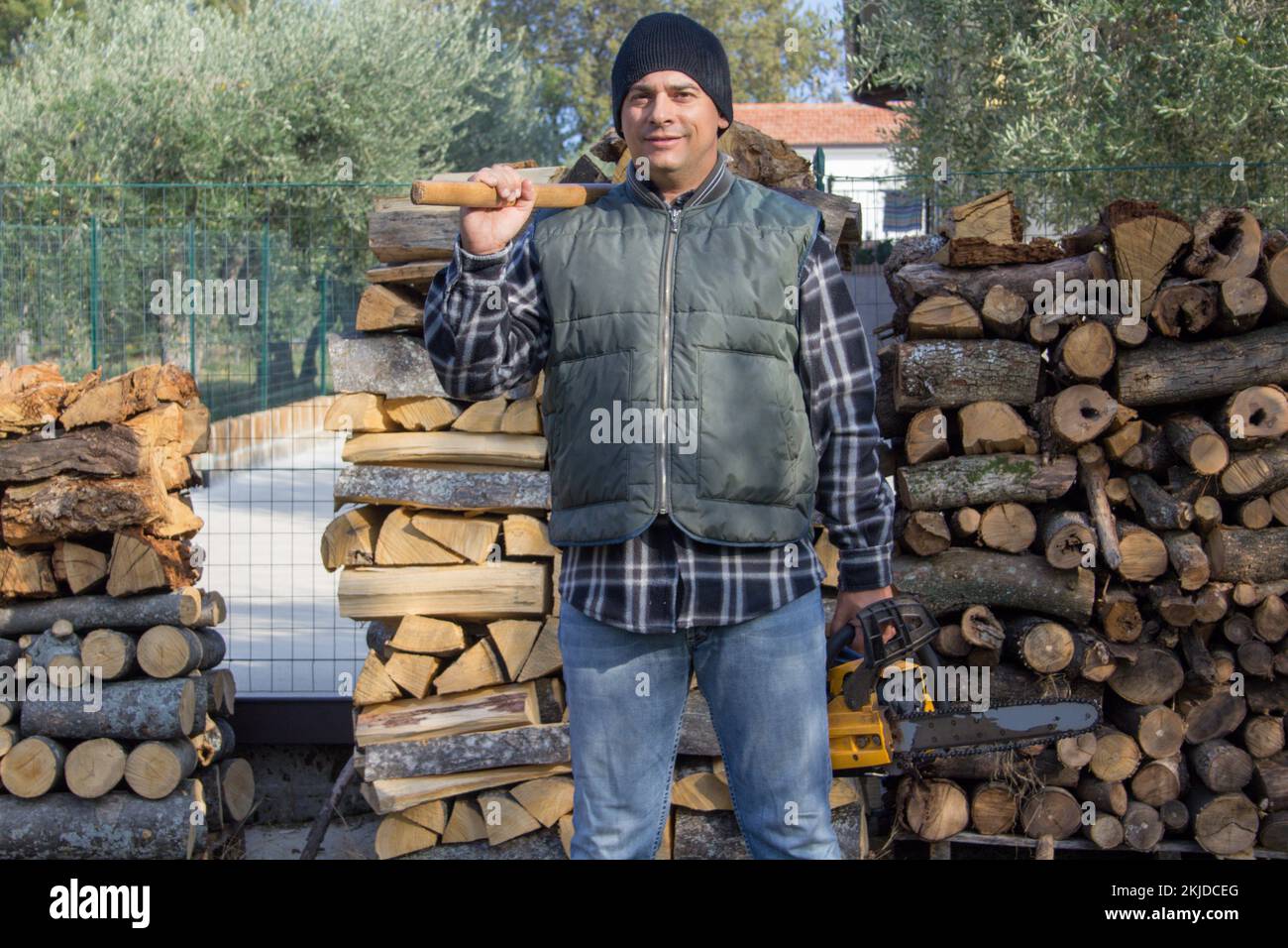 Smiling lumberjack with ax on shoulder and chainsaw in hand after ...