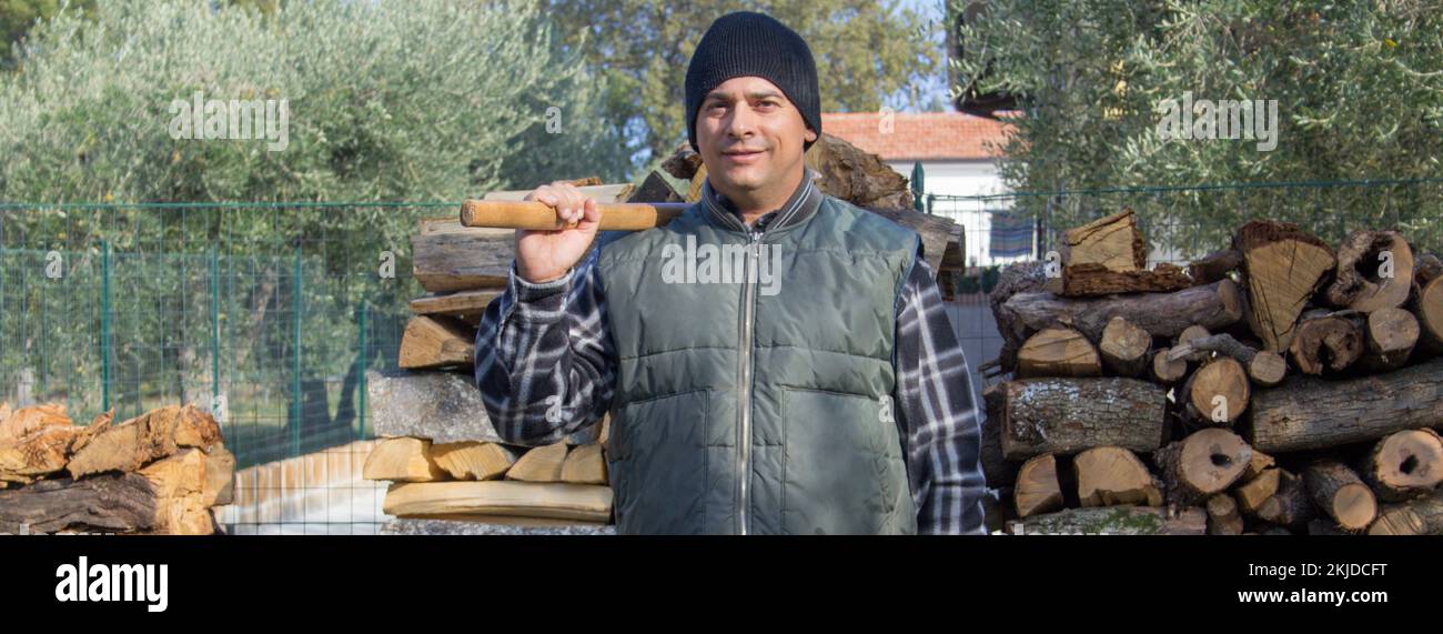 Smiling lumberjack with ax on shoulder and chainsaw in hand after ...