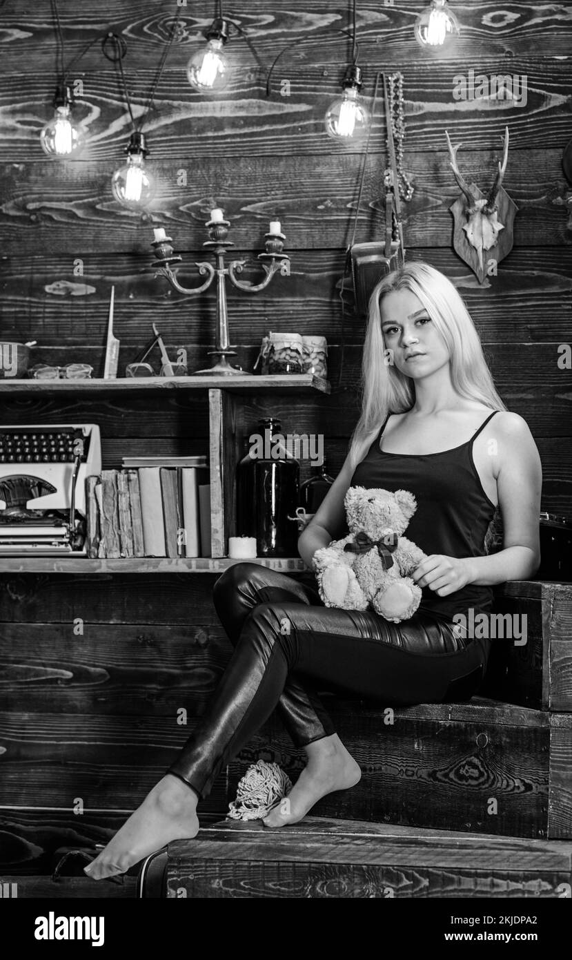 Girl in black clothes holds teddy bear toy in hand, wooden interior on ...