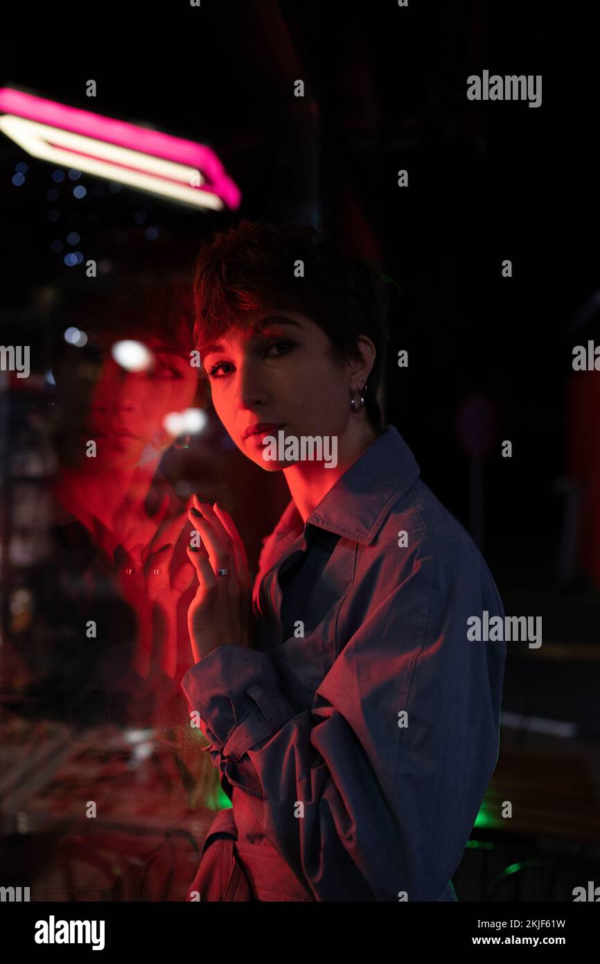 Sad lonely woman in red neon light leaning on shop window on street at ...