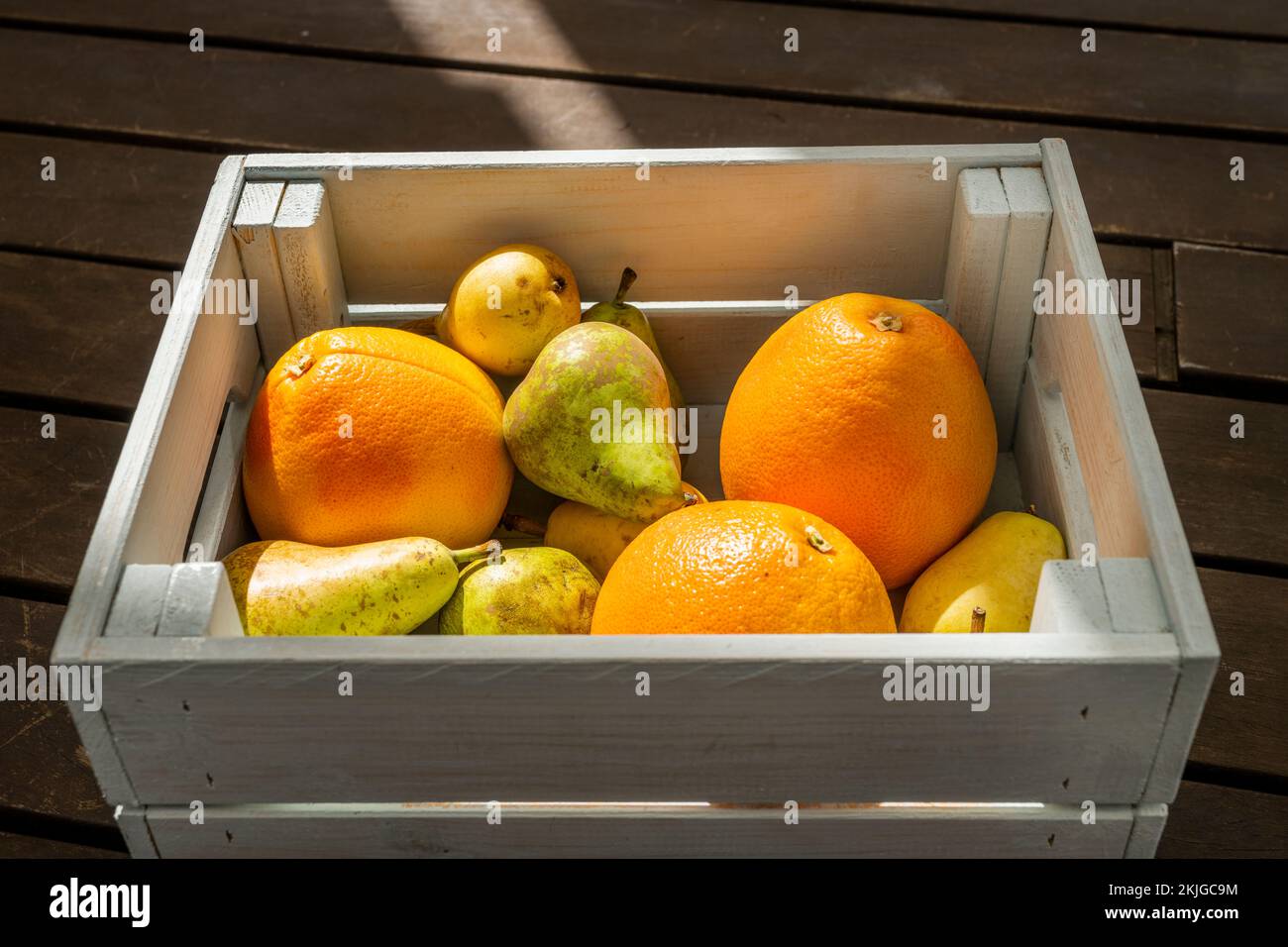 A wooden crate filled with ripe citrus and assorted pears bathed in ...