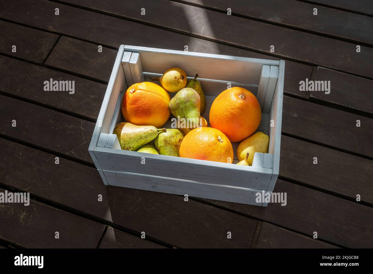 A wooden crate filled with ripe citrus and assorted pears bathed in the ...