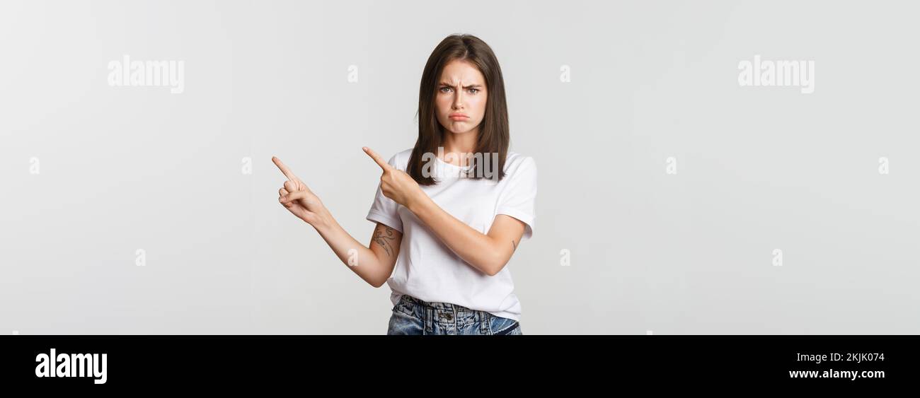 Disappointed sulking girl pointing fingers upper right corner, frowning ...