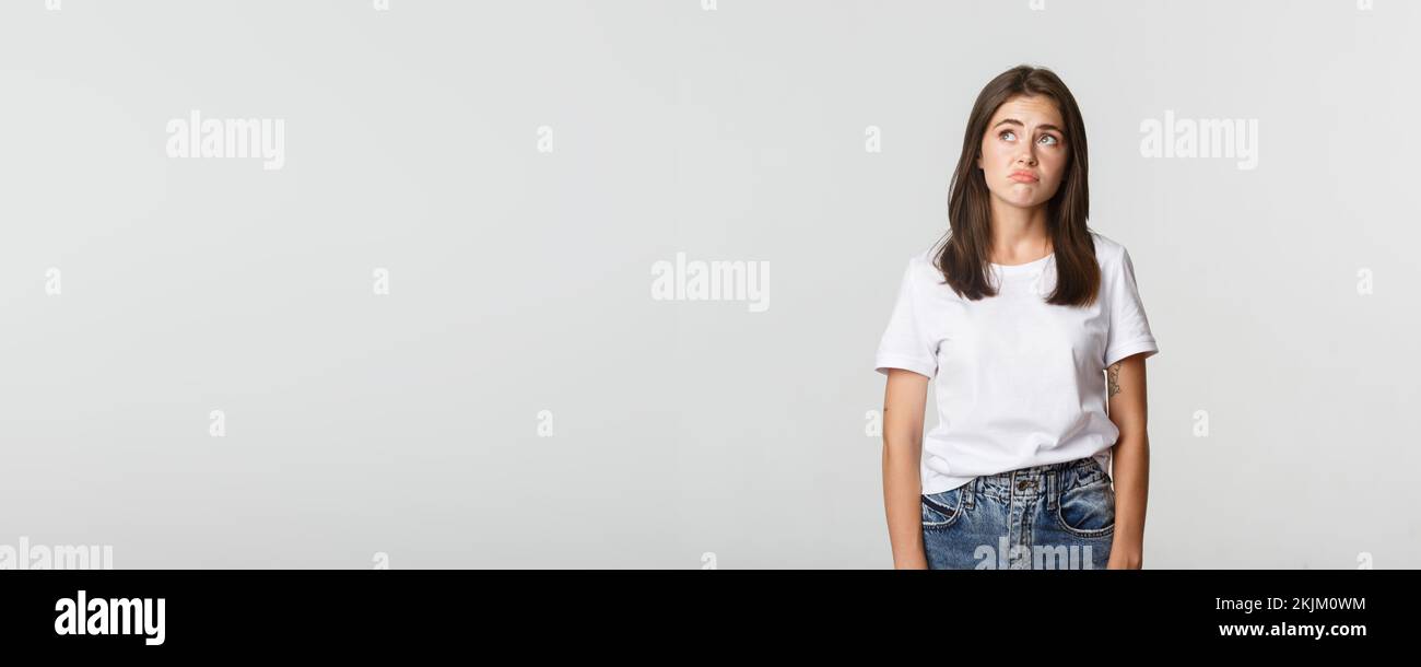 Sad cute girl sulking, feeling regret and looking upper left corner ...