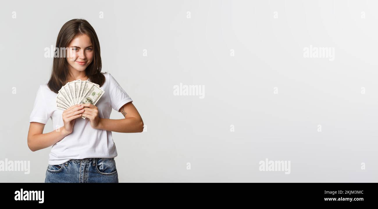Greedy smiling girl looking cunning and holding money, standing white ...