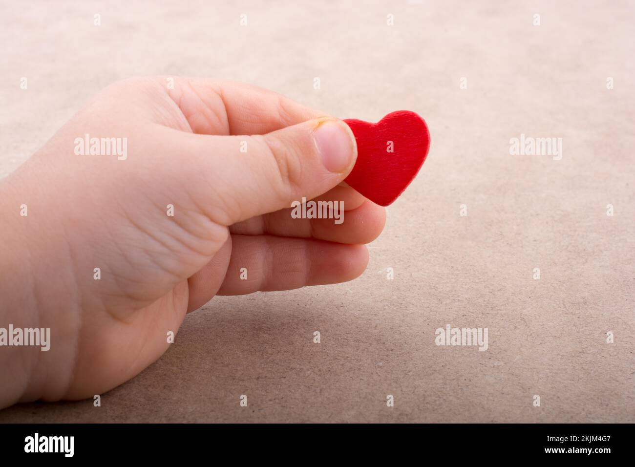 Little red color heart shape in hand on light brown background Stock ...