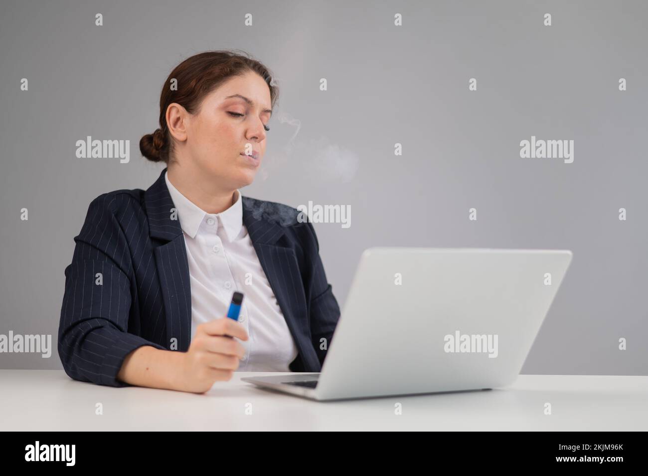 Business woman smoking a disposable vape while sitting at her desk ...