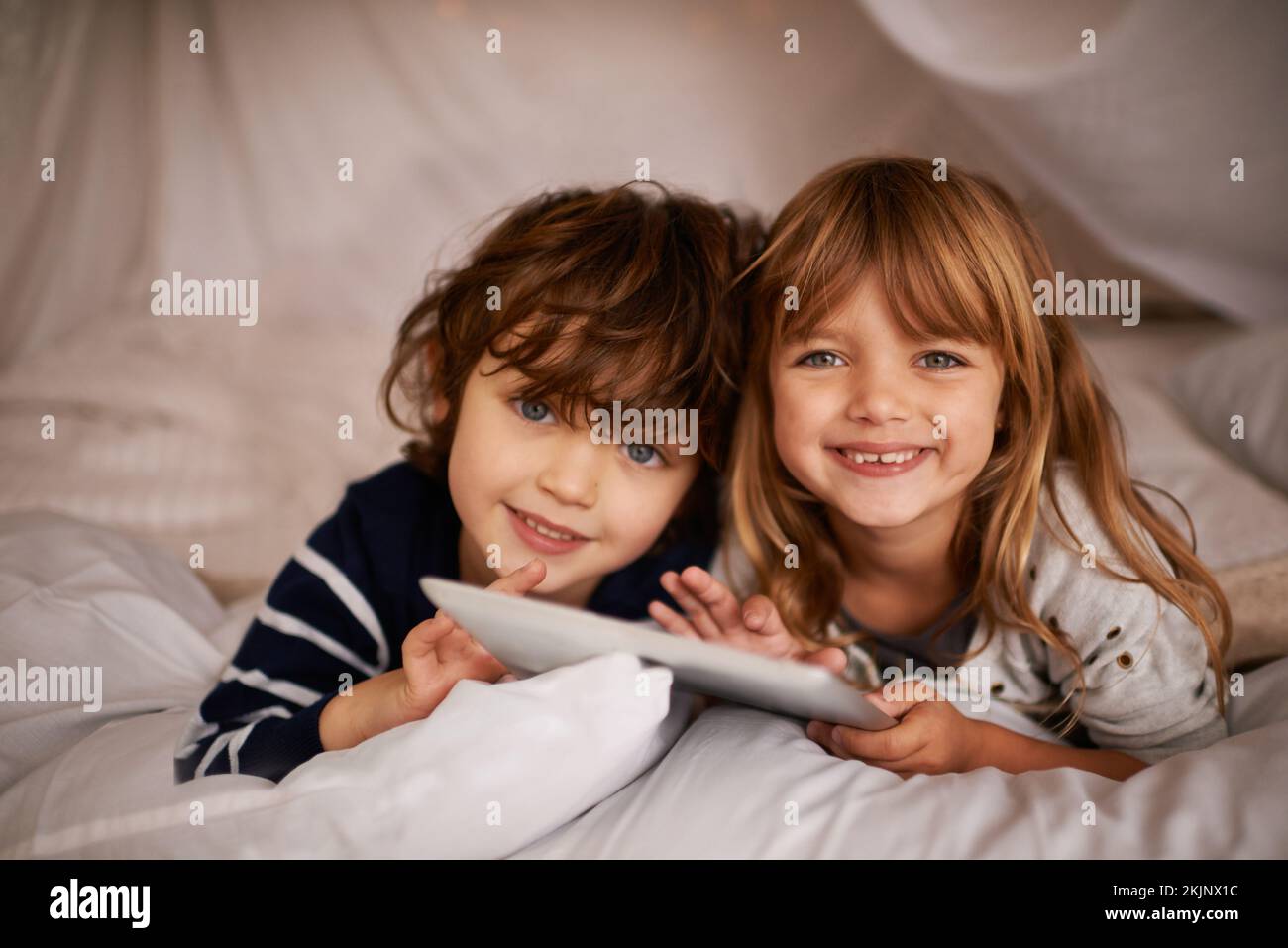 Sibling solidarity. Portrait of two adorable siblings lying underneath ...