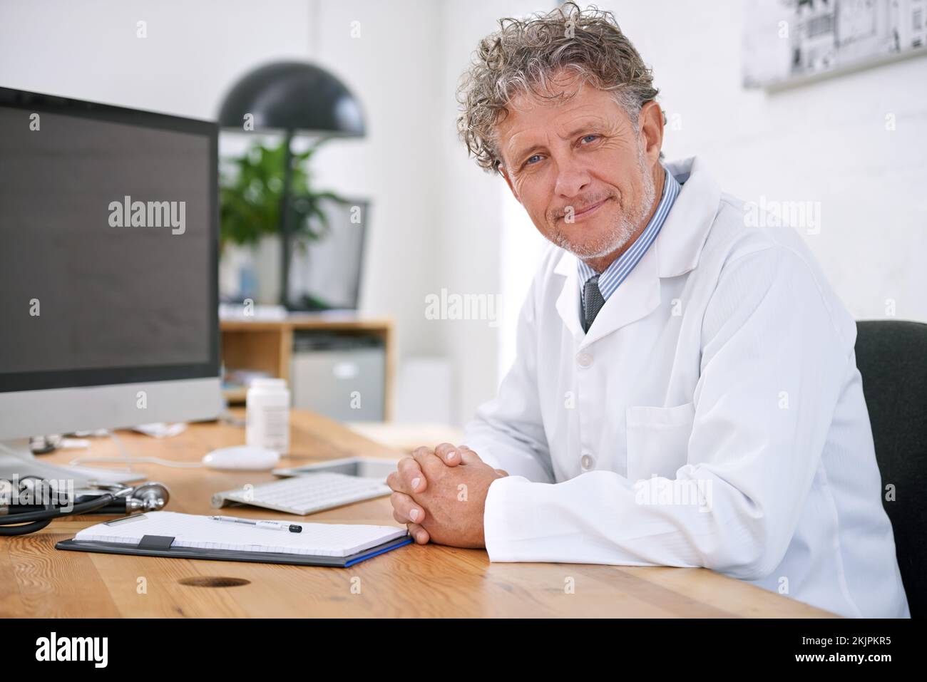Tell me where it hurts. Portrait of a smiling mature doctor sitting at ...
