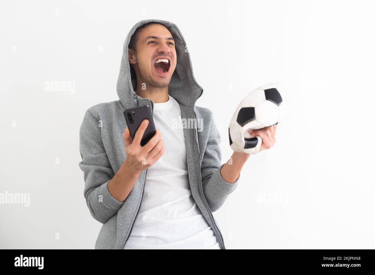 Young man football fan in shirt support team with soccer ball sit sofa ...