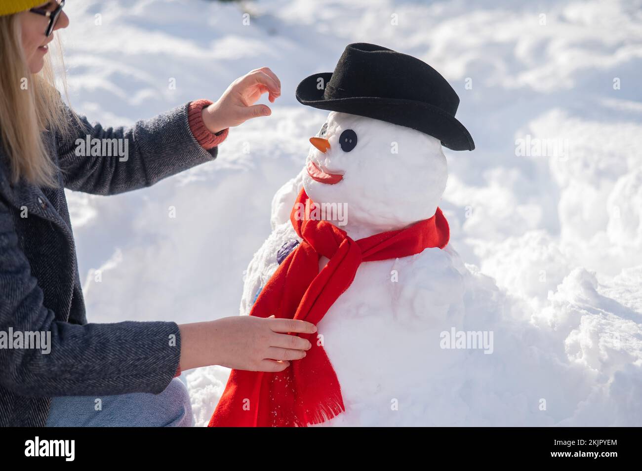Caucasian woman sculpts a snowman from the snow. The carrot is the ...