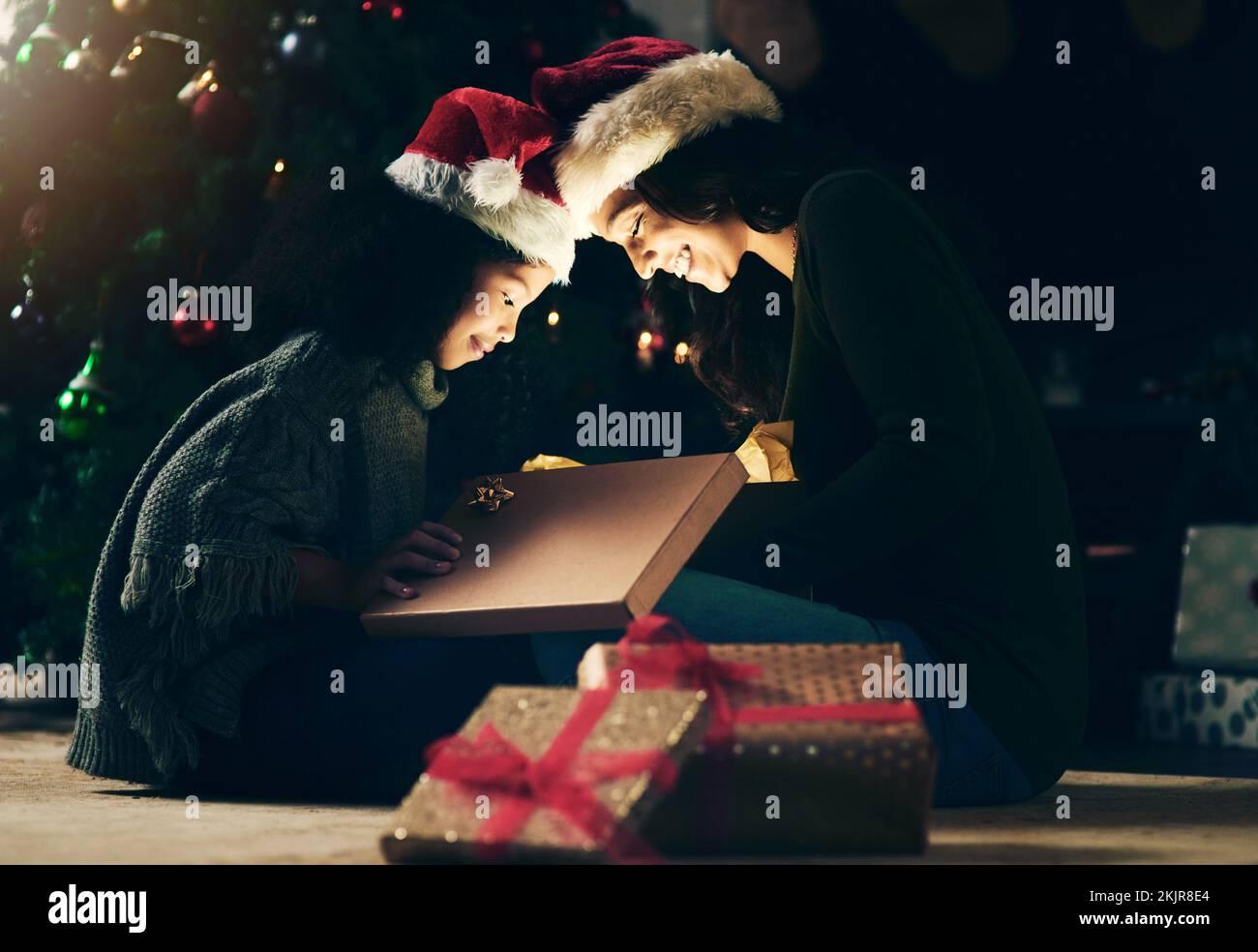 Mother, child and opening Christmas gift together at night, excited and ...