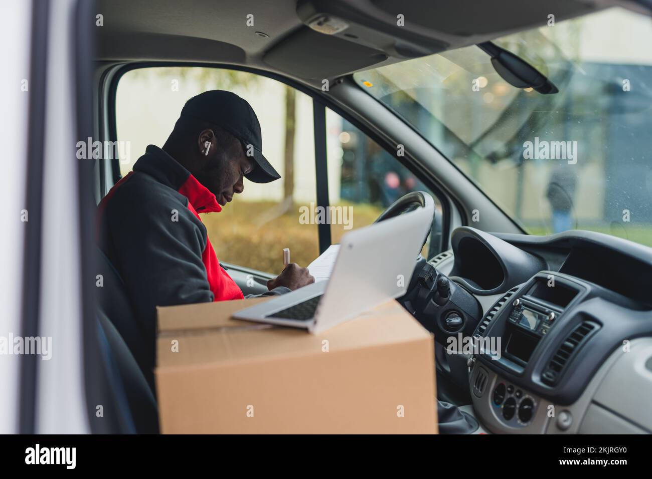 Black young adult delivery guy sitting inside white van signing papers ...