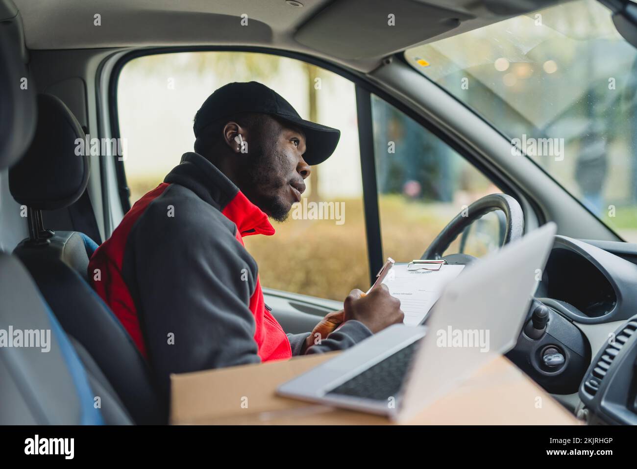 Young adult black delivery man sitting in driver seat of van holding ...